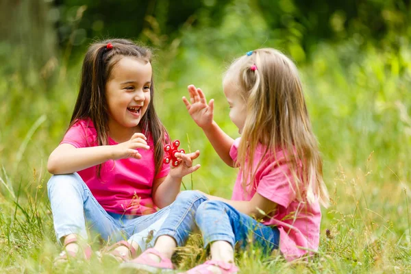 Two cute little sisters having fun while sitting on the grass on a ...