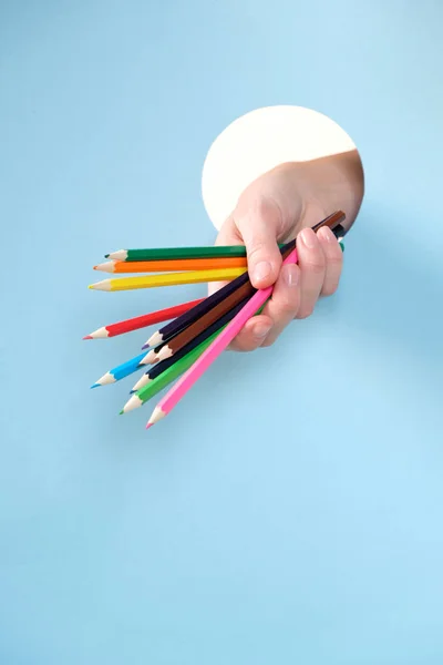 Human hand protruding through hole in blue background, holding colored ...