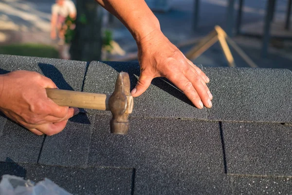 Roofer with hammer in motion, laying asphalt shingles tiles on house ...
