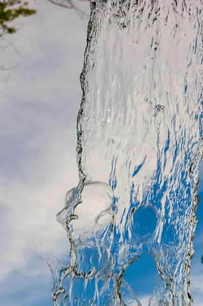 transparent falling water vertical flows against a blue sky and green ...