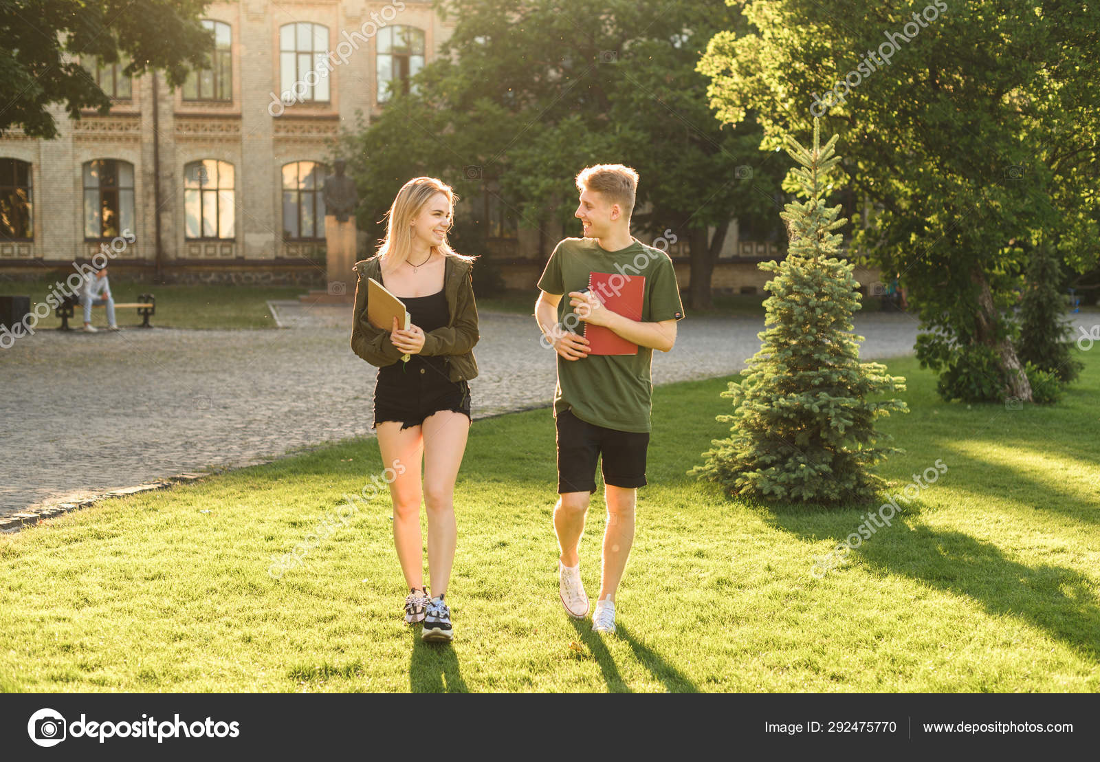 Two students, female and male, cheerfully walk in the university park ...