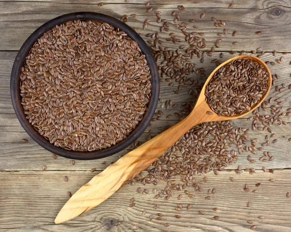 Flax seeds in bowl with scattered grains on wooden background with wooden spoon. Also known as ...