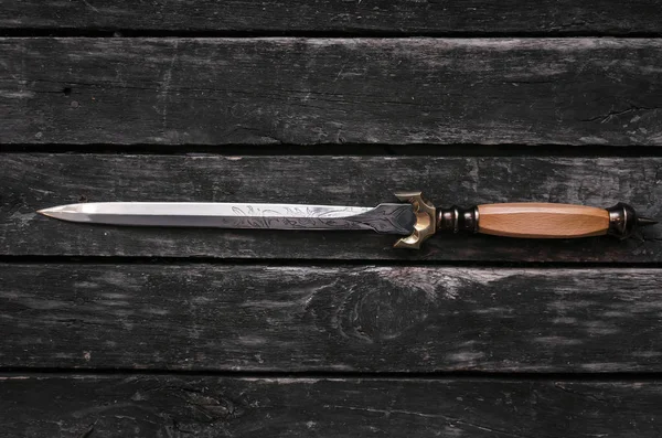 Dagger blade on aged wooden table background with copy space. Assassin ...