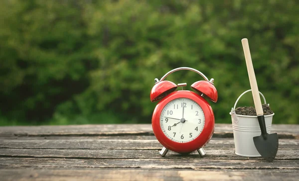 Red alarm clock, bucket with a soil and a shovel on a garden wooden ...