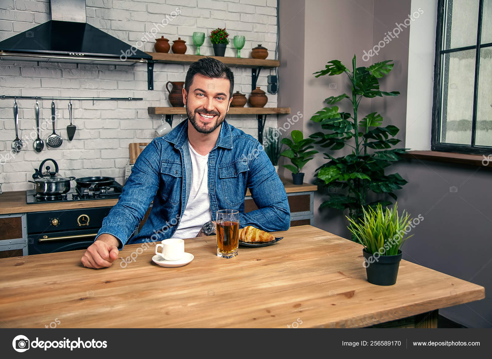 Handsome young smiling guy is home at his kitchen eating breakfast ...