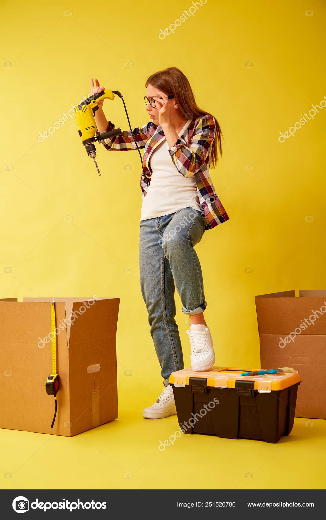 Girl scared holding a drill, standing between the boxes. Studio Stock ...