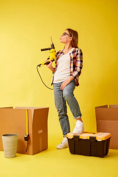 Girl scared holding a drill, standing between the boxes. Studio Stock ...