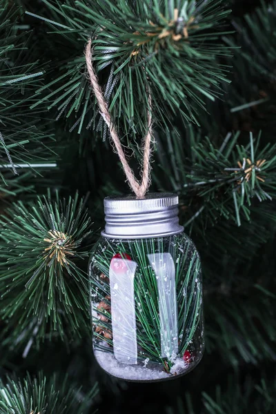 Bank with spruce branch on Christmas tree. Glass New Year toy on branch ...