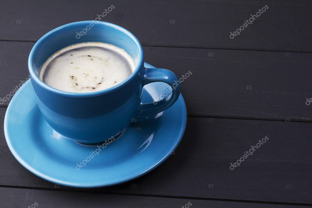Café en taza azul con plato que le hace juego en fondo de madera negra 2022