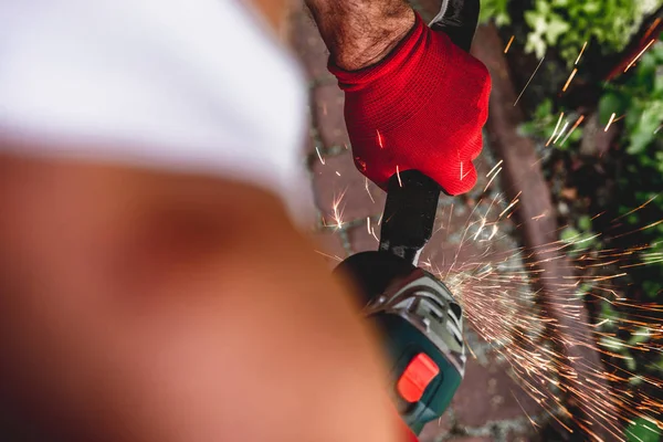 The man is sharp with the mower's knife with a grinder, sparks fly from ...