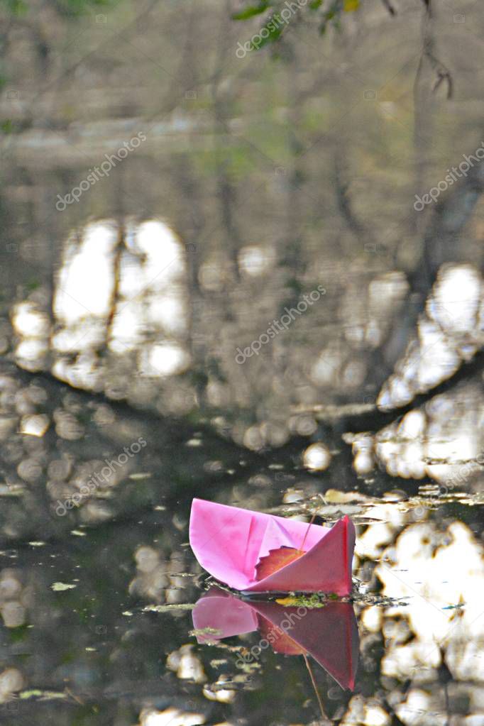 Un barco de papel autoplegado flota en el suelo en otoño en un charco ...