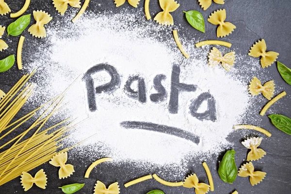 Pasta written in a heap of flour, with different varieties of pasta ...