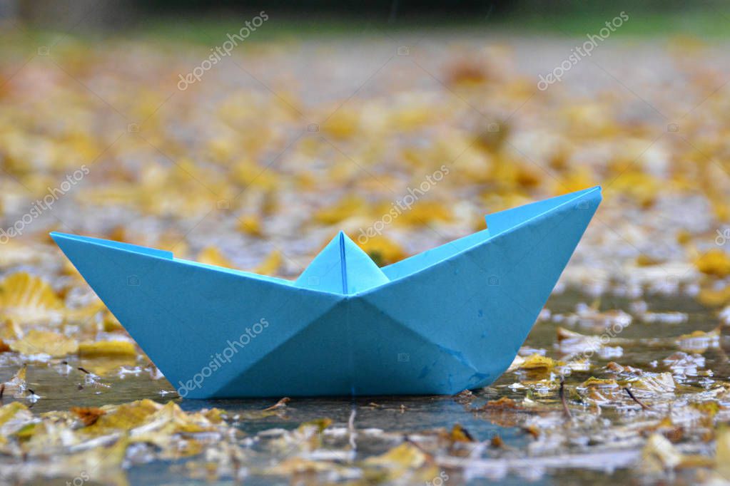 Un barco de papel autoplegado flota en el suelo en otoño en un charco ...