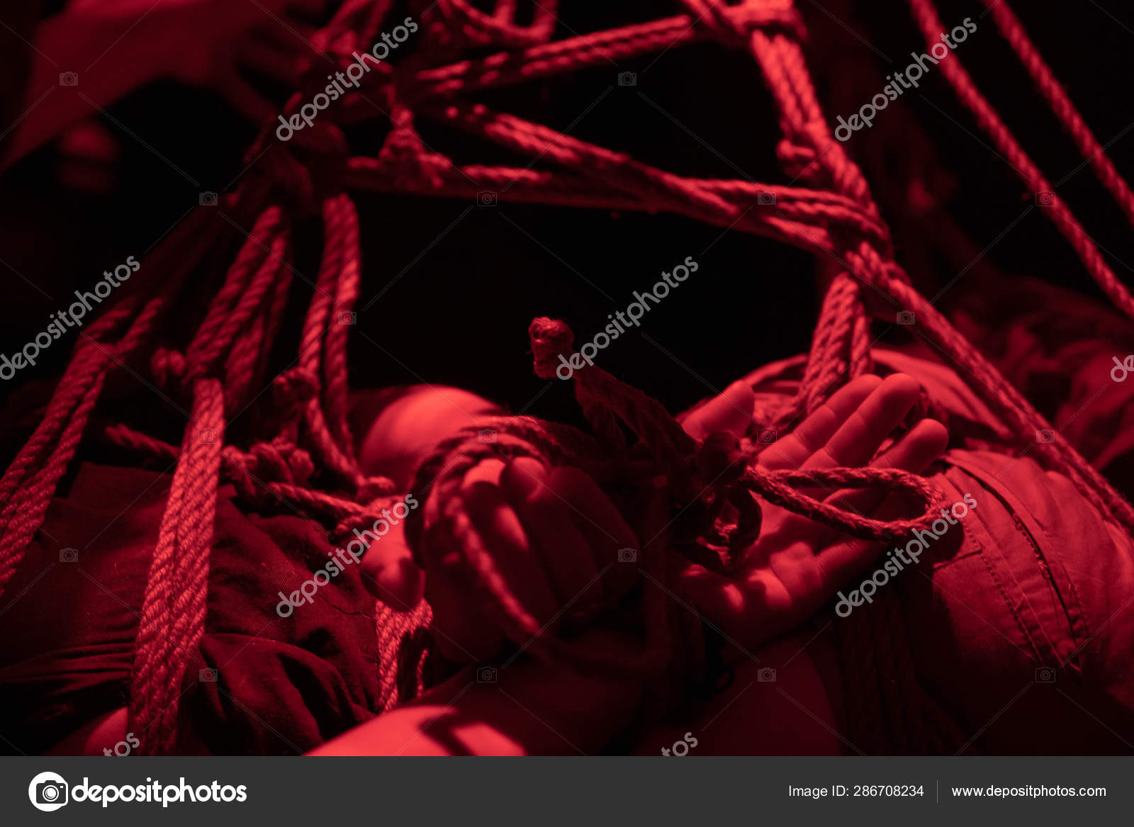 Female domination shibari performance in red erotic light. Bonded hanging man receive punishing ...