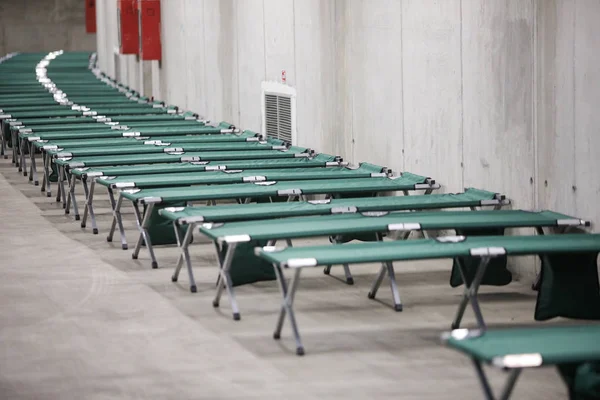 Camp folding cots are being set up in the underground parking of a ...