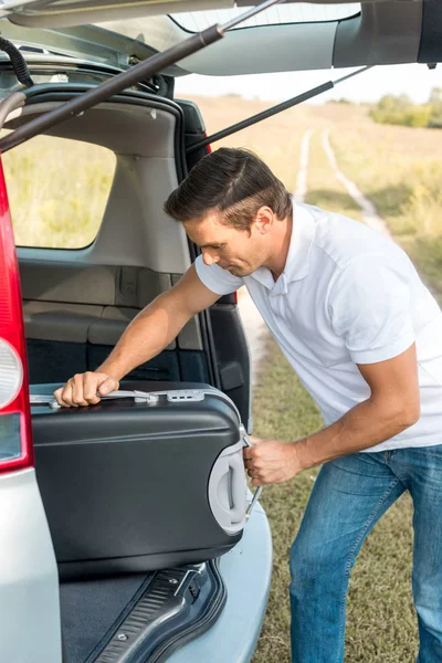handsome man packing suitcase into luggage boot of car in field - Stock ...