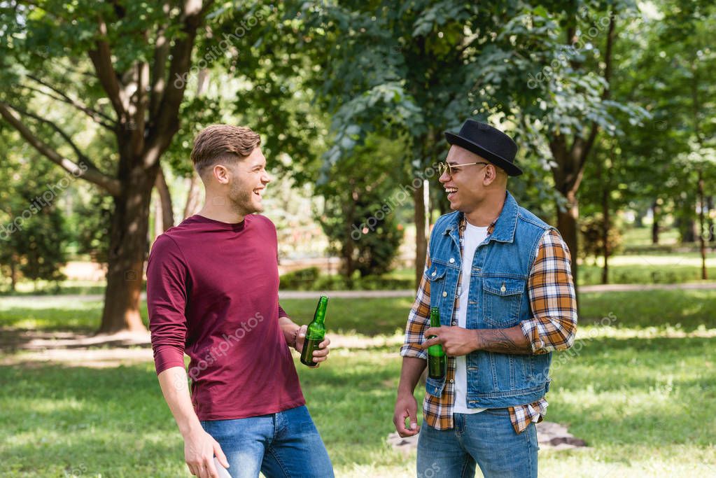 alegres hombres multiculturales sonriendo mientras sostienen botellas ...