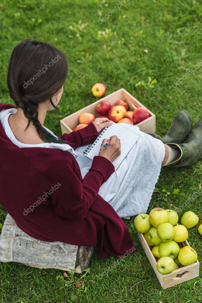 vista trasera de la niña escribiendo en bloc de notas y sentado en el ...