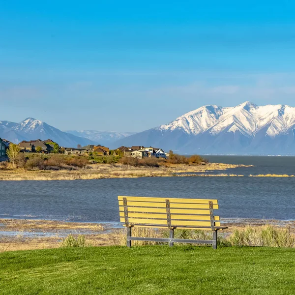 Square Bench on grassy terrain facing a lake with houses built near its ...