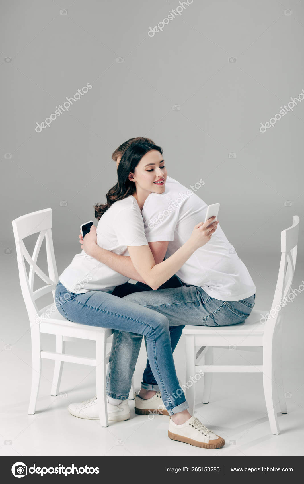 Young Couple Embracing While Sitting White Chairs Using Smartphones ...