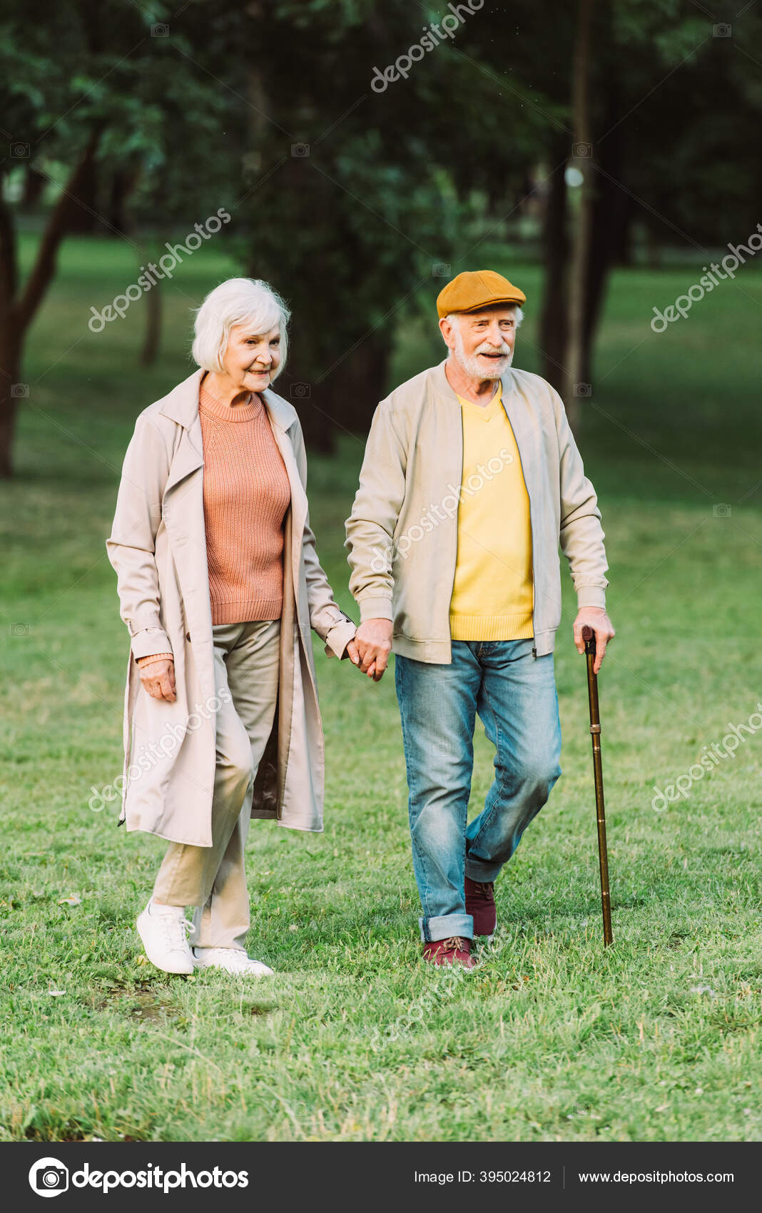 Smiling Elderly Couple Holding Hands While Walking Grassy Meadow Park