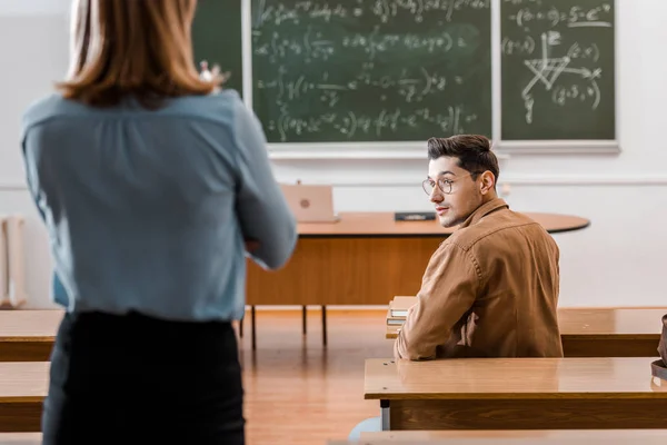 back view of female teacher looking at male student sitting at desk ...