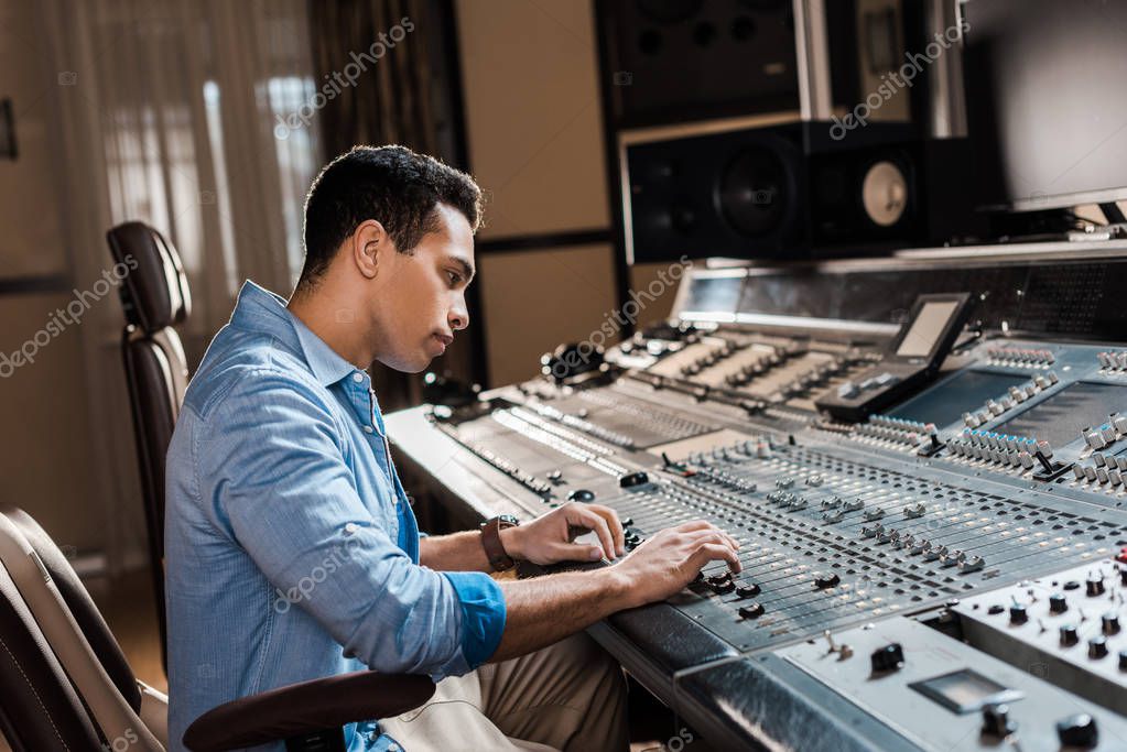 productor de sonido de carrera mixta atento trabajando en la consola de mezcla en el estudio de ...