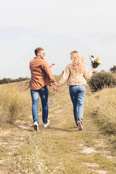 back view of woman with bouquet and man holding hands - Stock Image ...