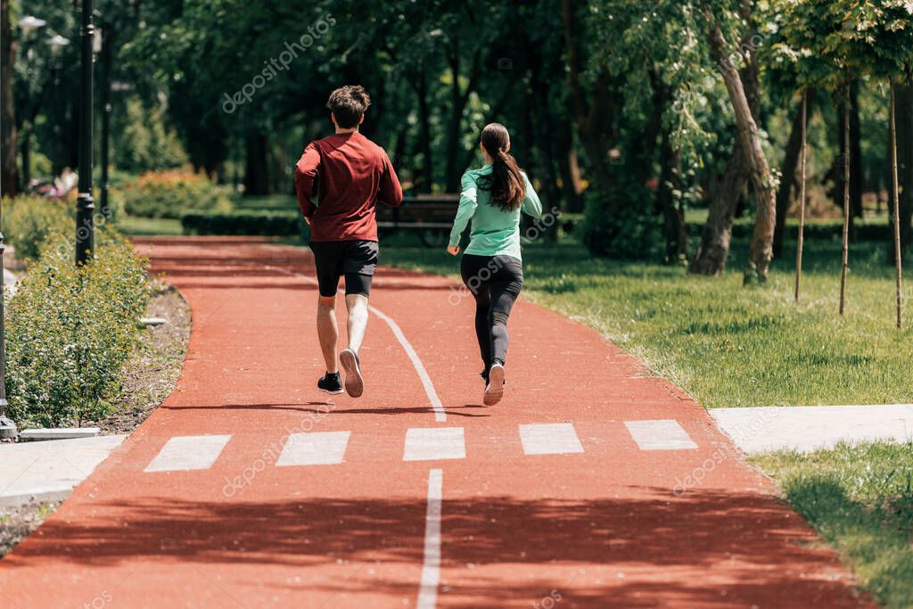 Vista trasera de la joven pareja corriendo juntos en pista de atletismo ...