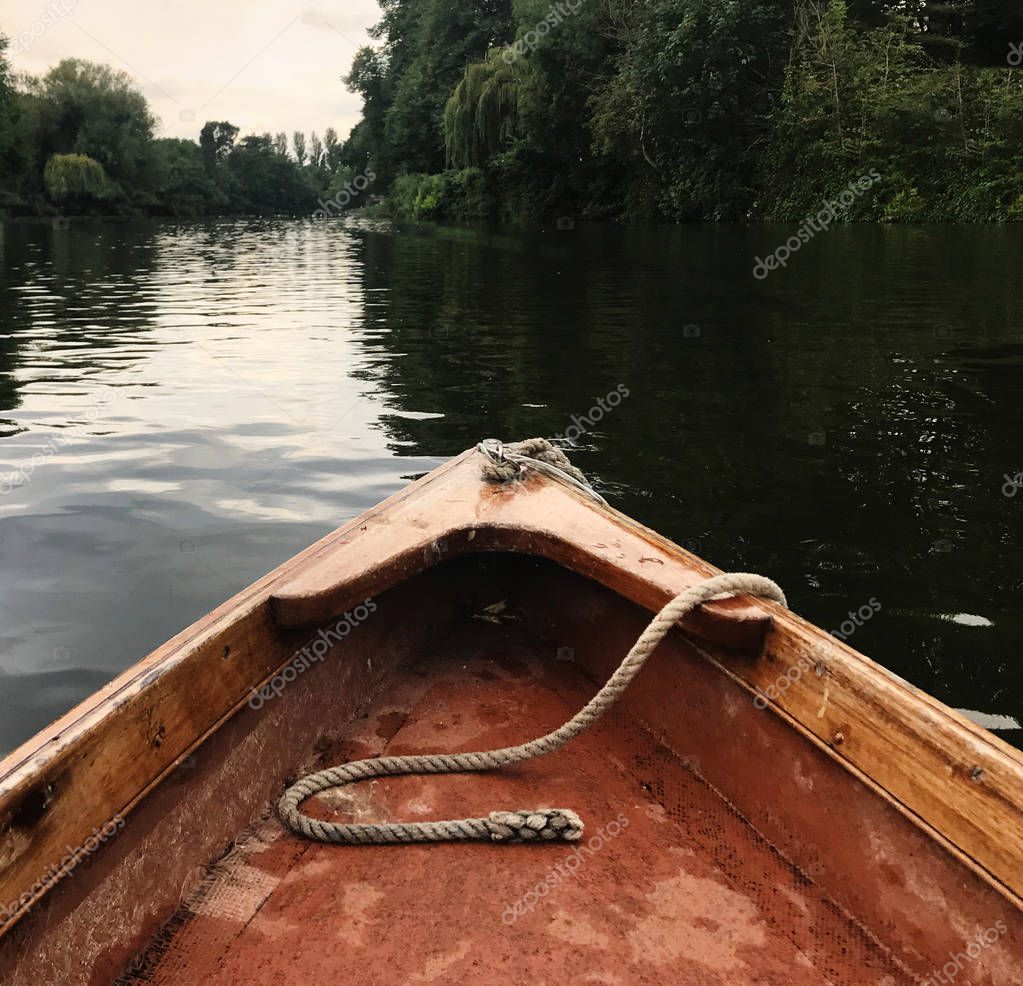 Barco de remo de madera en el río, cuerda rústica, ondulaciones de agua ...