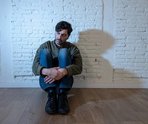 young depressed man sitting against a white wall at home with a shadow ...