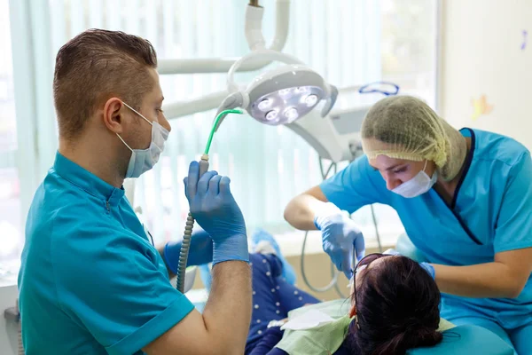 Dentist at work in dental unit with a nurse and a woman lying patient ...