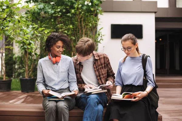 Group of students sitting on bench and reading books in courtyard of ...