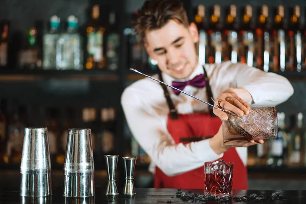 Barman holding a long spoon and glass filled with ice cubes on the bar ...