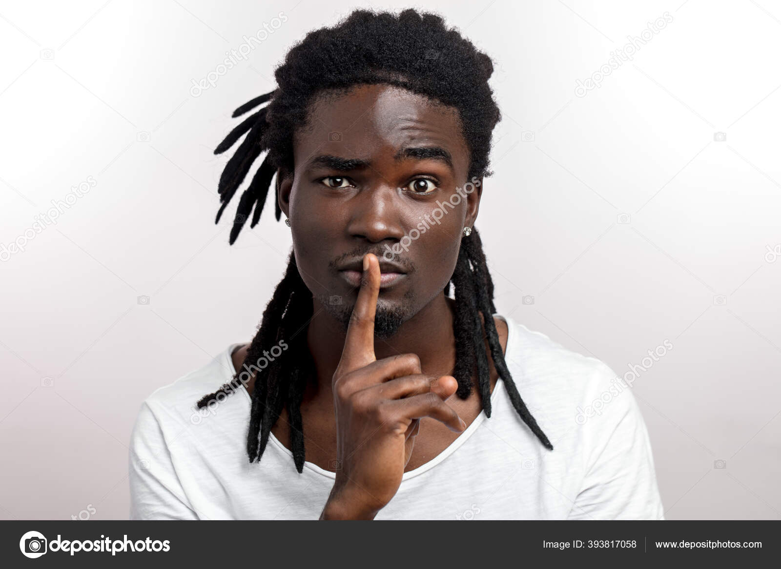 Dark-skinned young man gesturing as secret holding his index finger at ...