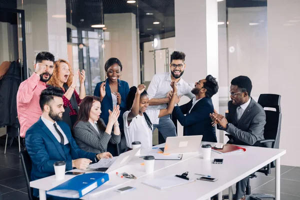 Young multi-ethnic work team exchanges ideas gathering around laptop ...