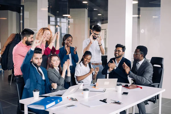 Young multi-ethnic work team exchanges ideas gathering around laptop ...