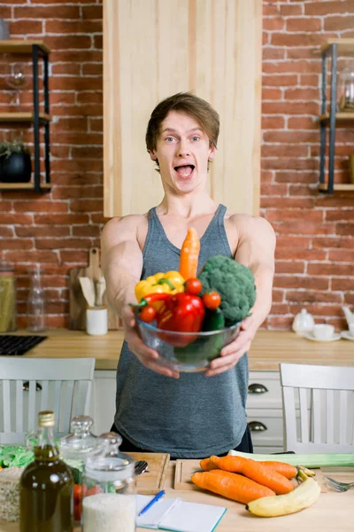 Handsome young cheerful man in sport clothes holding bowl with healthy ...