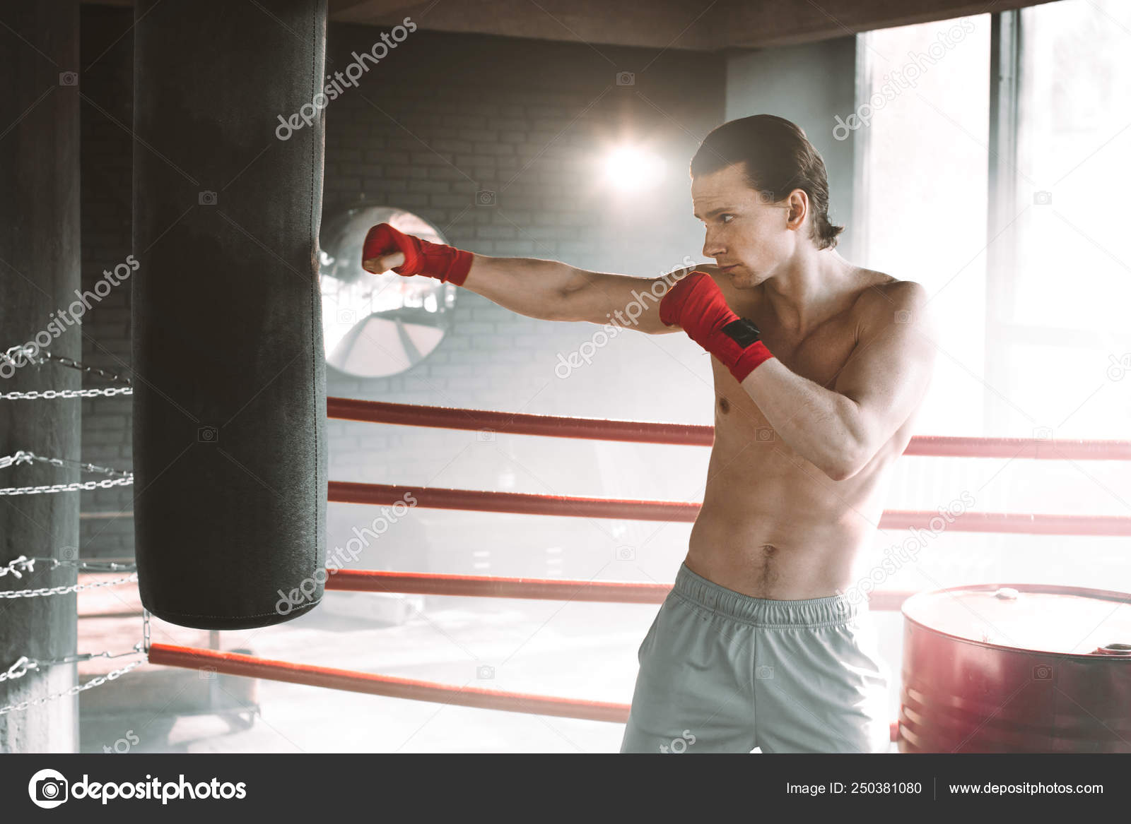 Angry boxer standing in boxing pose near punching bag on black with ...