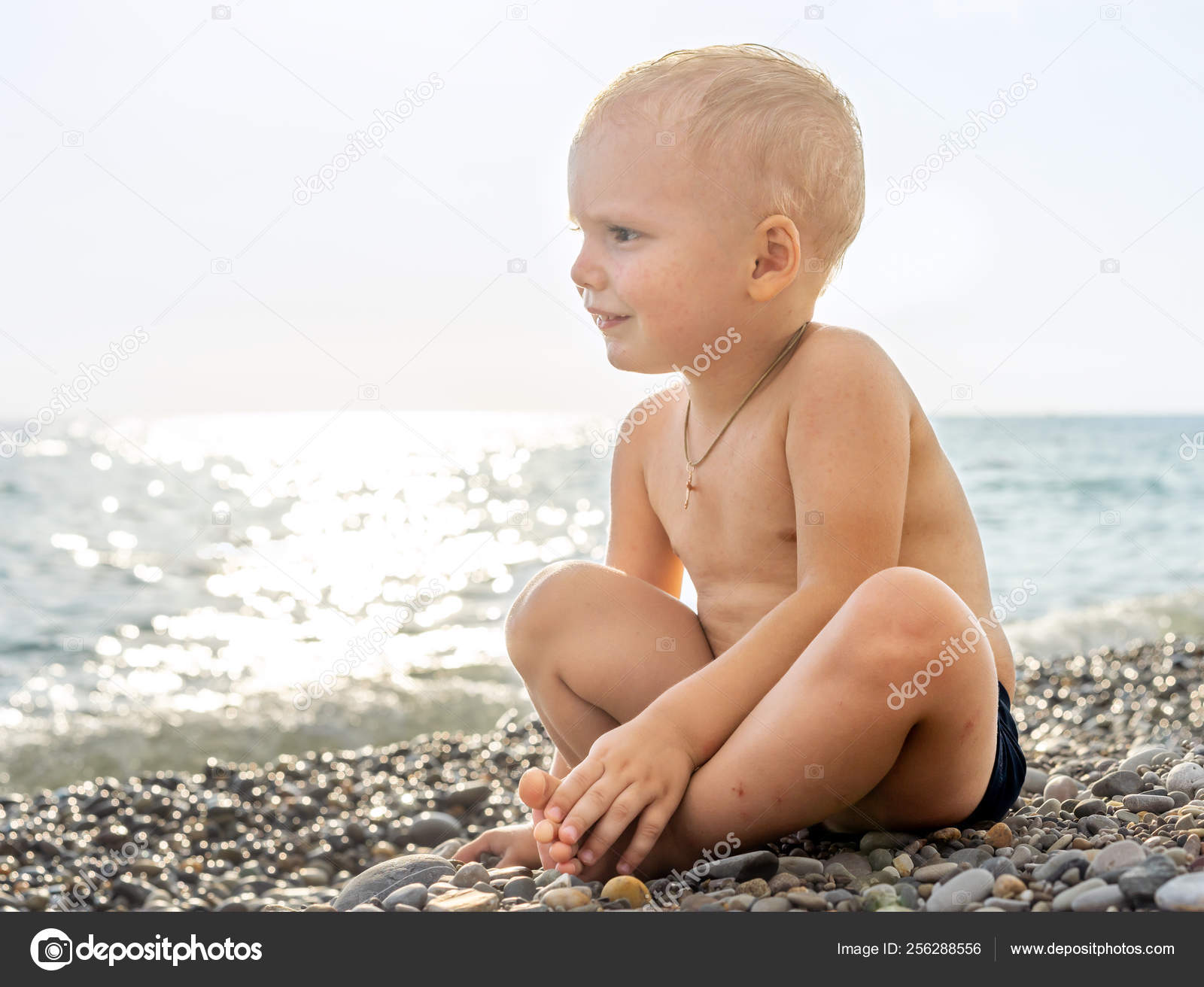 Beautiful boy sitting on pebbles near the sea ⬇ Stock Photo, Image by ...