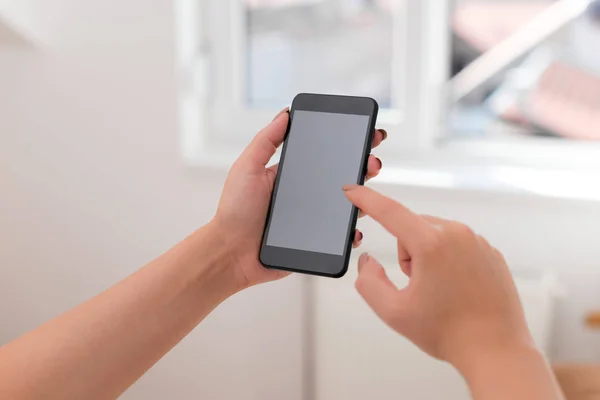 Young lady using a dark smartphone inside home in a wooden desk. Woman ...