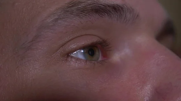 Close-up of a mans human eye. the man looks closely at the TV screen ...