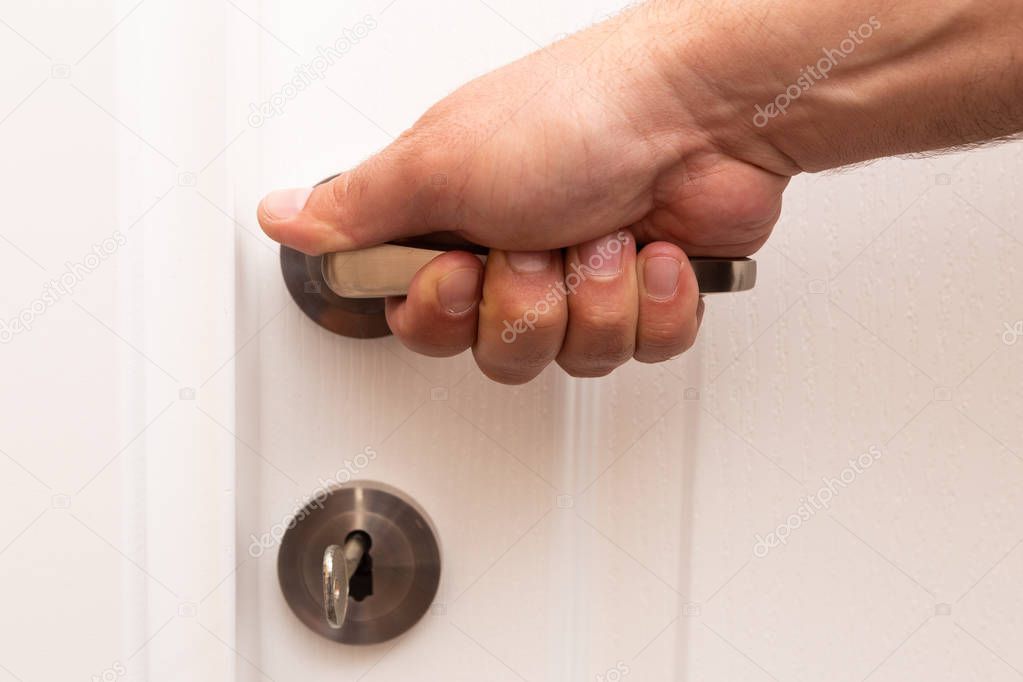 Mano que toca la manija metálica de la entrada de madera blanca 2023