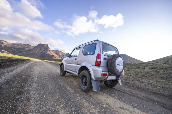 Rear view of small 4x4 on dirt road driving toward mountain highlands ...