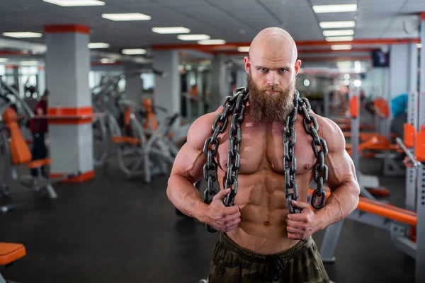 A bald, bearded bodybuilder with large relief muscles holds a heavy ...