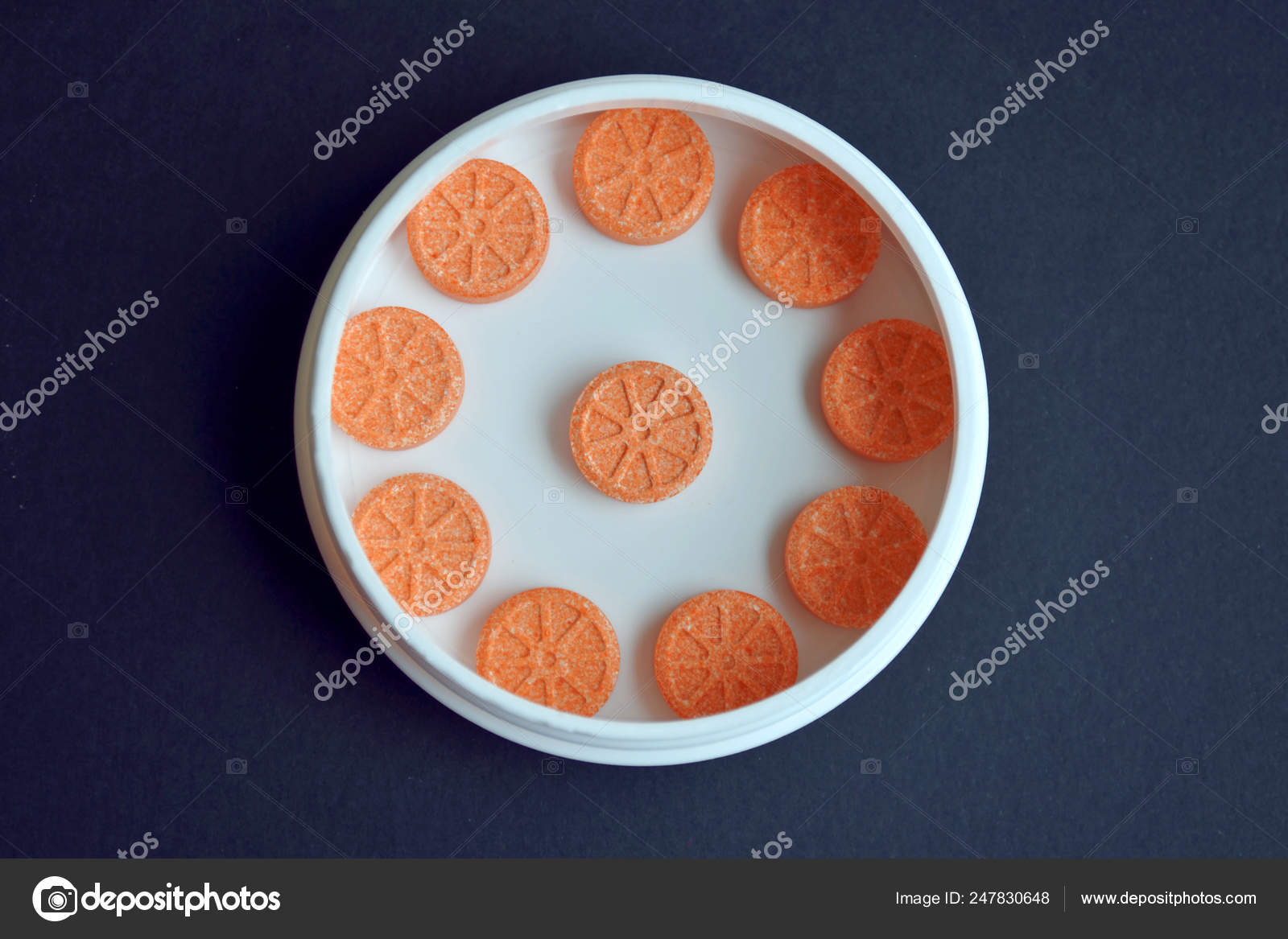 Orange round tablets in the shape of an orange lie in a round white jar ...