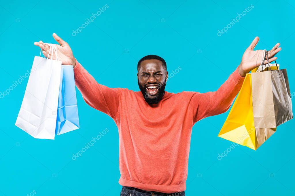 Grandes compras. Feliz hombre afroamericano de pie sobre fondo azul ...