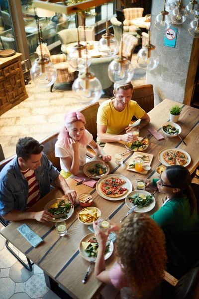 Five young friends sitting by large served wooden table and enjoying ...