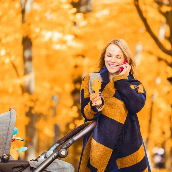 A young mother with a stroller is talking on her mobile phone while ...