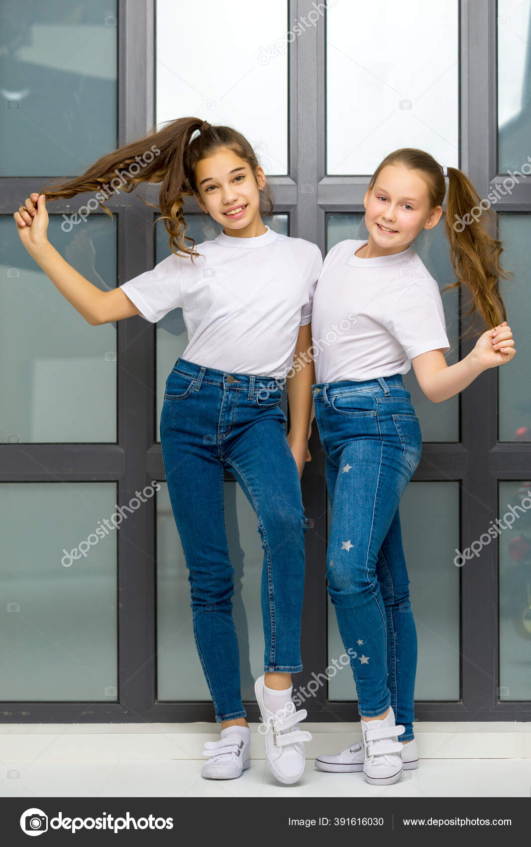 Zwei süße kleine Mädchen posieren im Studio neben einem großen Fenster ...